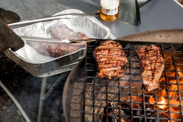 BBQ grilling meat beef steaks on a cast iron grill over the campfire ...