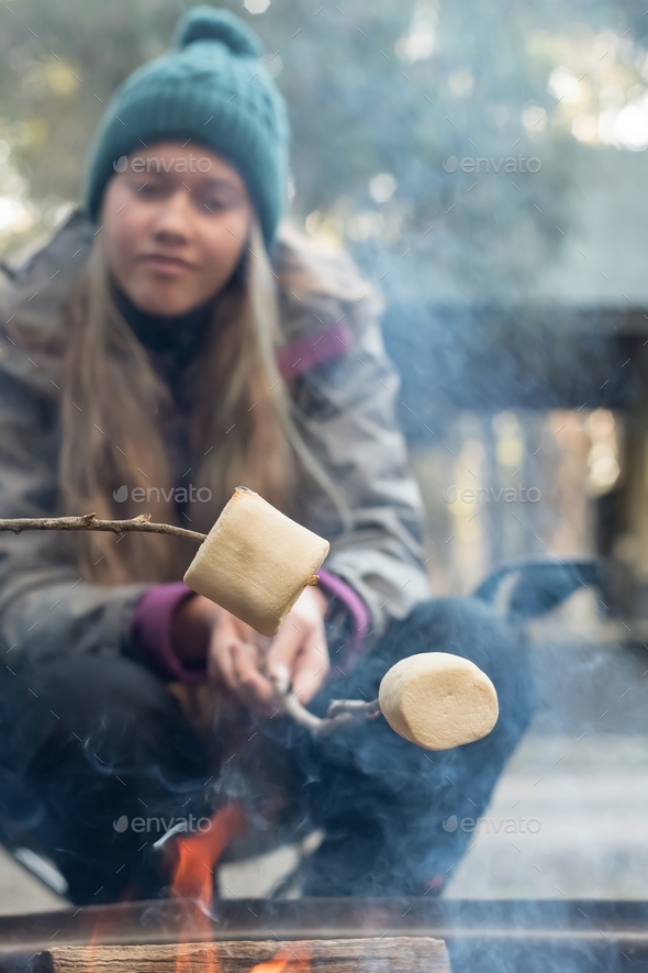 Teenage girl roasting big marshmallows on a stick over the campfire. Camping family fun Stock ...
