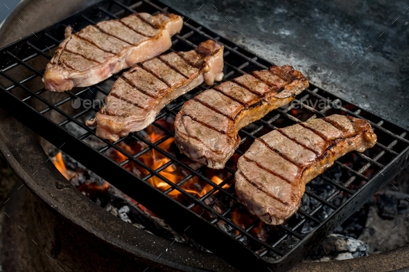 BBQ grilling meat beef steaks on a cast iron plate over campfire ...