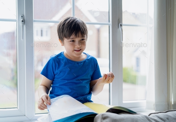 Kid sitting next to window reading a book with bright light shining ...