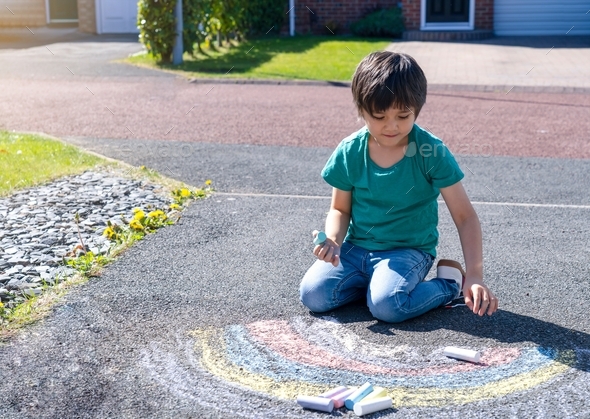 Kid colouring rainbow on pavement, Child drawing rainbow with chalks on ...