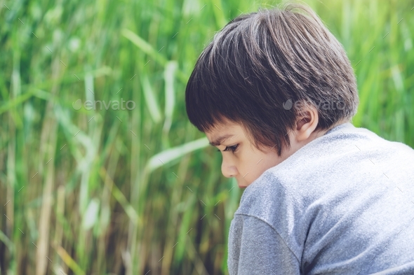 kid sitting alone at grass field.Child looking down with curious face ...