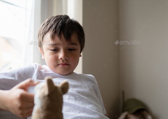 Happy Child boy with smiling face sitting on sofa playing with dog toy with lighting shining ...