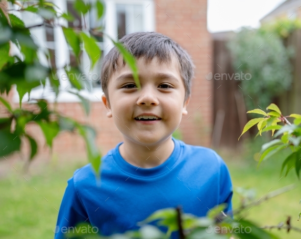 Happy boy standing behind tree in the garden,Smiling kid playing ...