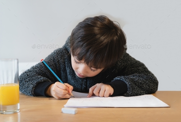 Kid siting on table doing homework,Child boy holding pencil writing on ...