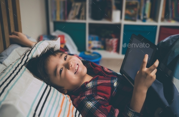 Happy boy lying in bed watching stories on internet, cute Child reading ...