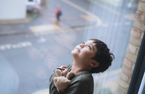 Young kid standing next to window looking up to sky with smiling face ...