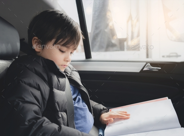 Kid siting on car seat and reading a book, Young boy sitting in safety ...