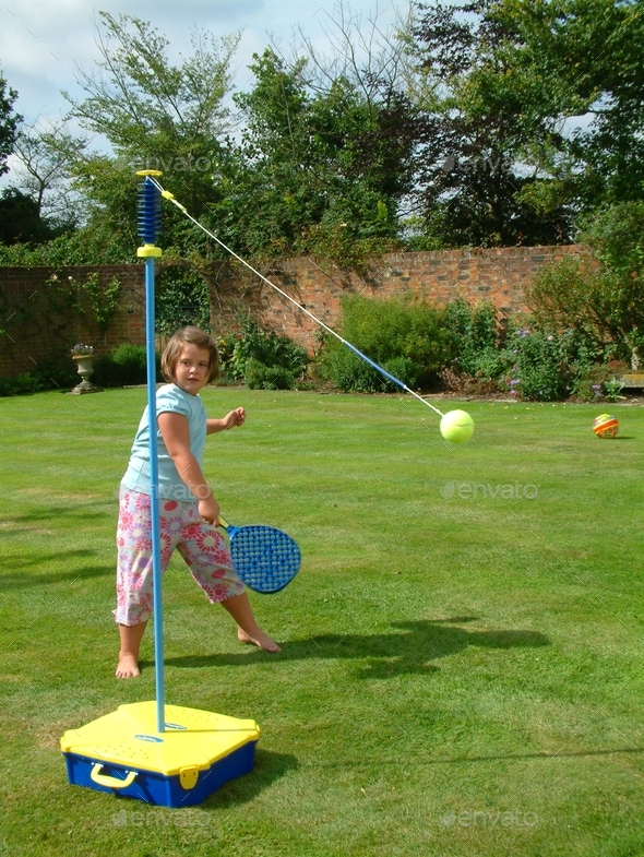 Little girl in walled country garden. Playing a game with a bat and ...