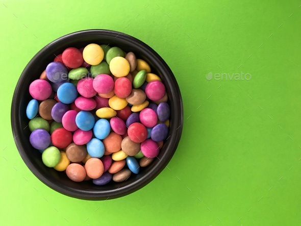 Multicoloured candies in a round dish, on a lime green background with ...