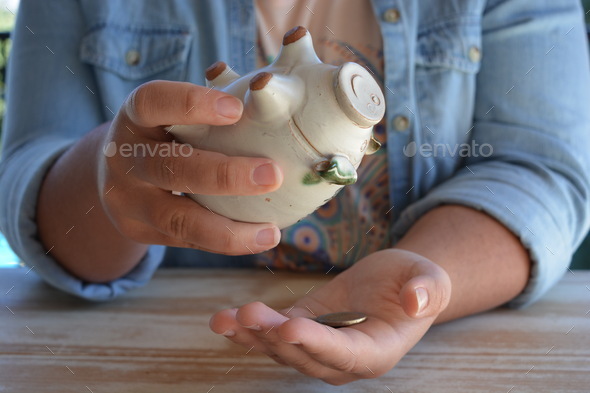 Girl tipping coins out of piggy bank into her hand, counting her money ...