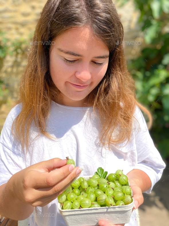 Young woman outdoors, holding fresh organic gooseberries in a recycled ...