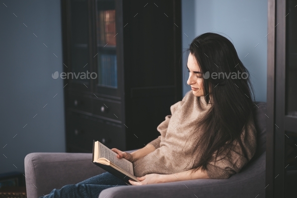 Beautiful dark haired woman takes book from book shelf and read it ...