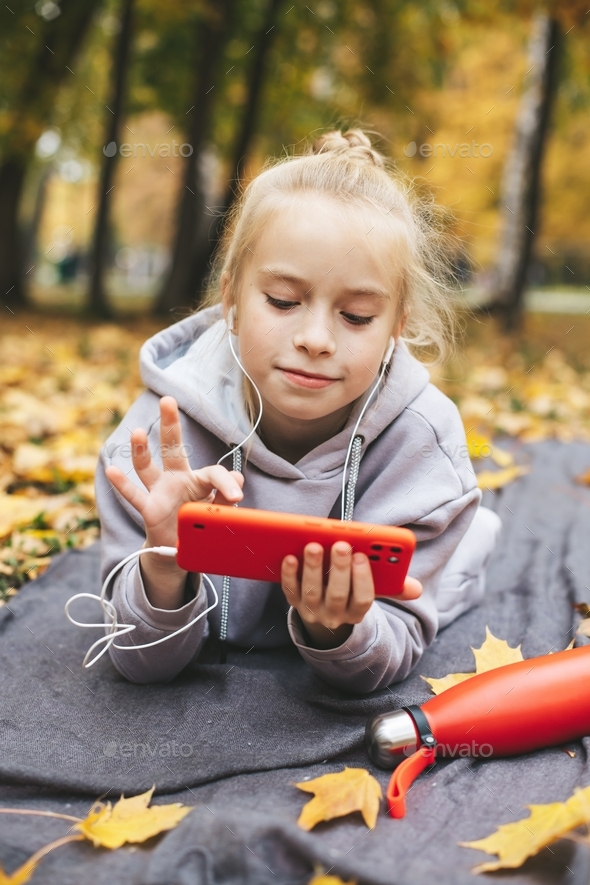 Happy blonde gen z girl sit on yellow autumn leaves with red bottle and ...