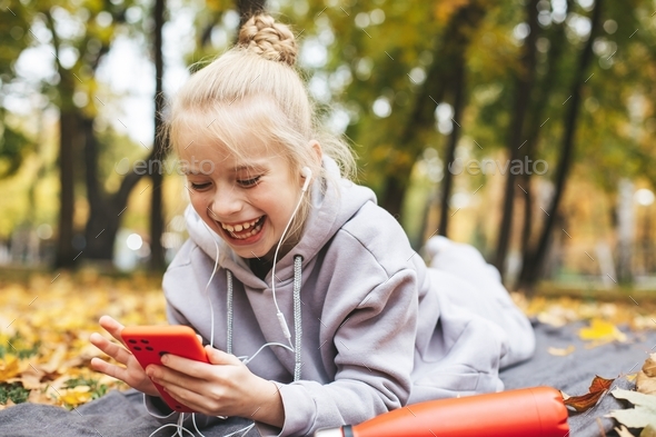 Happy blonde gen z girl sit on yellow autumn leaves with red bottle and ...