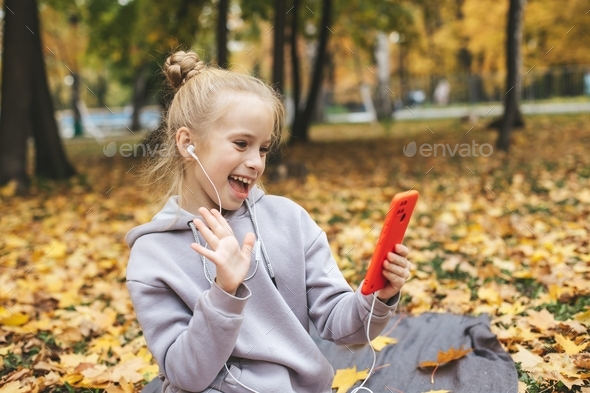 Happy blonde gen z girl lay on yellow autumn leaves with red bottle and ...
