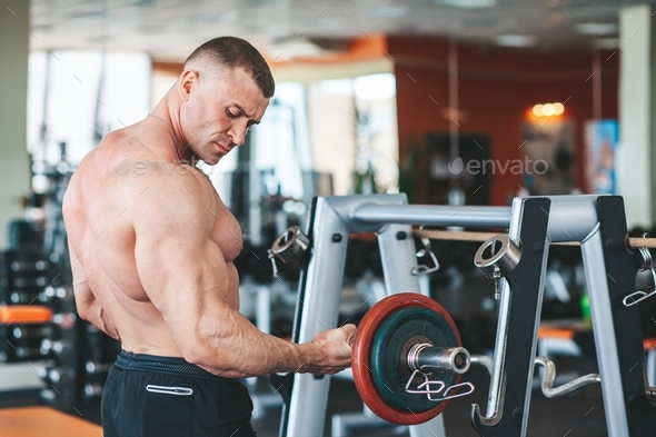 Muscular male bodybuilder training hard at gym using heavy barbells ...