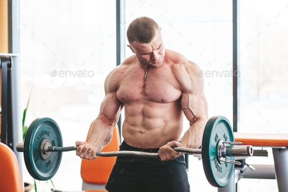 Muscular male bodybuilder training hard at gym using heavy barbells ...