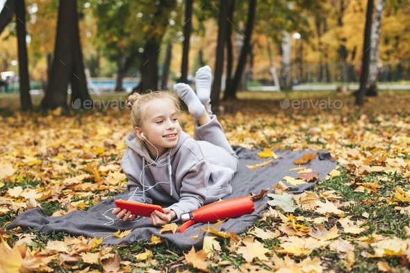 Happy blonde gen z girl sit on yellow autumn leaves with red bottle and ...