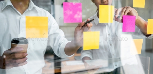 Young creative team professional using post it notes in glass wall to ...