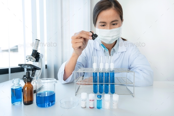 Scientist woman in medical face mask is using dropper to dropping ...