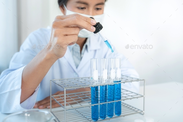 Scientist woman in medical face mask is using dropper to dropping ...