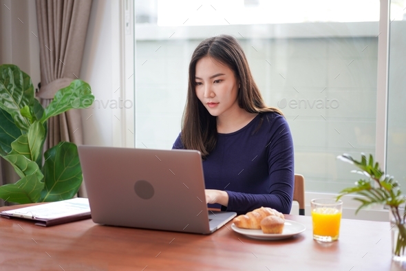 Young asian woman eating bread with a glass of orange juice while ...