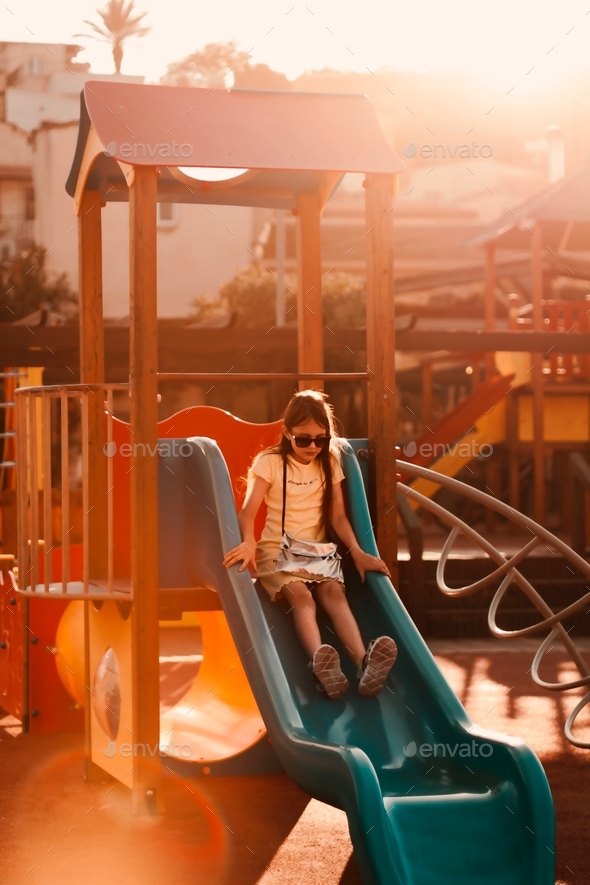 Teen girl going down the slide on playground. Golden hour natural light ...