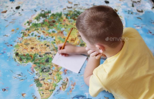 The child is at home lying on the floor and studying the world map ...