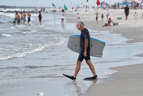 Senior baby boomer with boogie board at the beach wearing a short wet ...