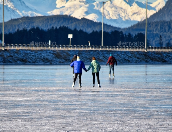 Ice skaters holding hands skating on a frozen lake in Alaska with snow ...