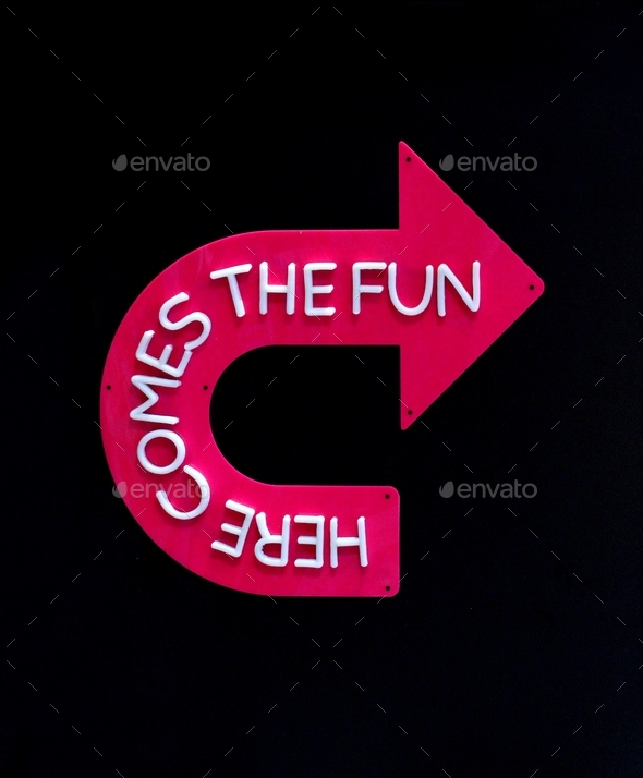 Here comes the fun! - glowing neon sign on a red arrow on a black ...