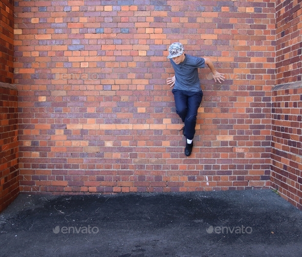 Teenage boy leaping in the air off a brick wall background, parkour ...