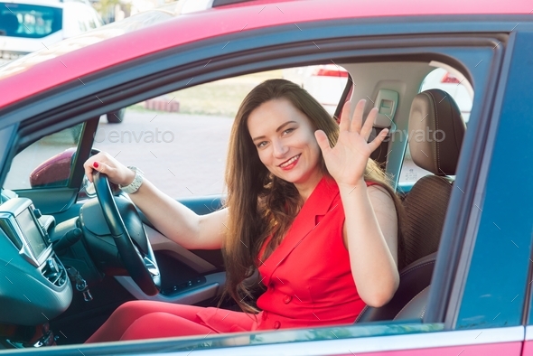 Portrait of smiling woman driver waiving hand while sitting behind the ...
