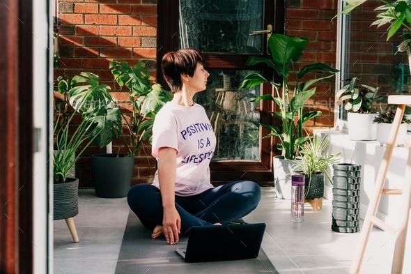 A woman on a mat doing twisting asana in a loft room with many green ...