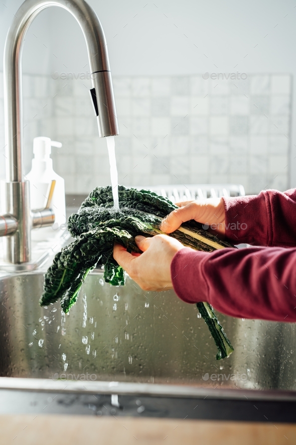 Woman washing kale underwater in the kitchen sink. Healthy eating ...