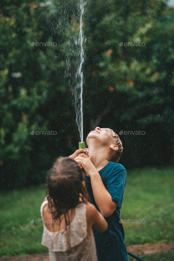 children splashing water from a hose Stock Photo by Yuliya_Kokosha