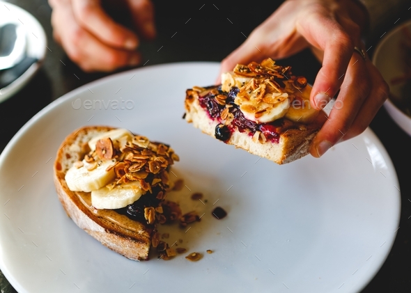 Woman’s hand holding toast with bananas and fruit and granola for a ...