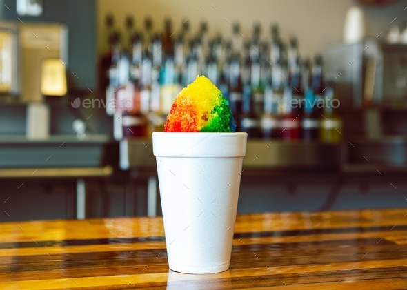 Colorful Rainbow shaved Italian ice in a white cup on a countertop, in ...