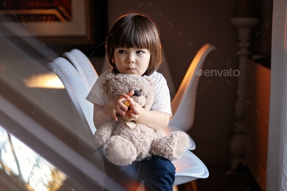 Little child sitting alone at home hugging his teddy bear. Punished and ...