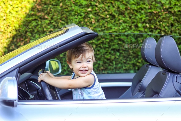 Happy little baby boy is driving the cabriolet car holding the steering ...