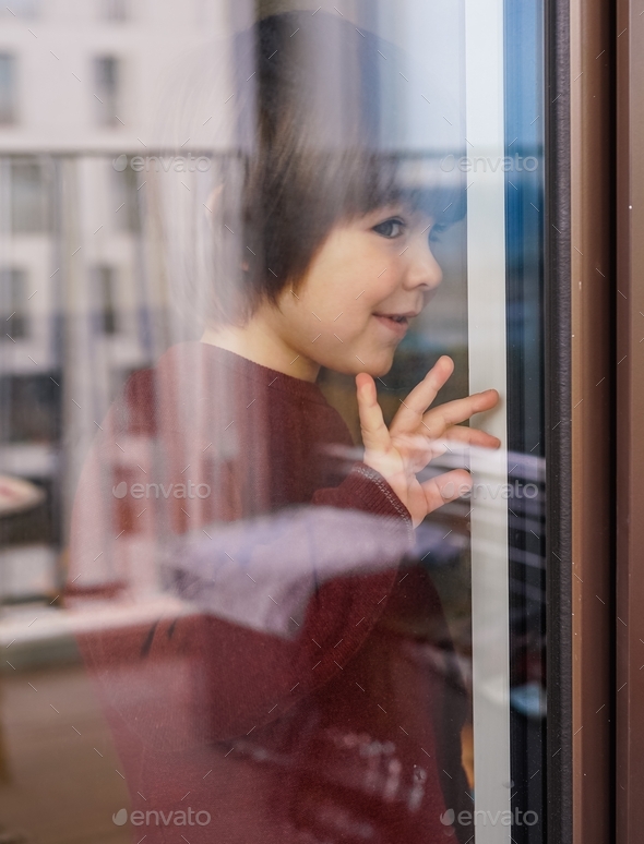 Smiling happy child looking through the glass window with city ...