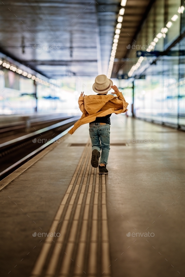 Back view of little child running after train on platform alone at ...