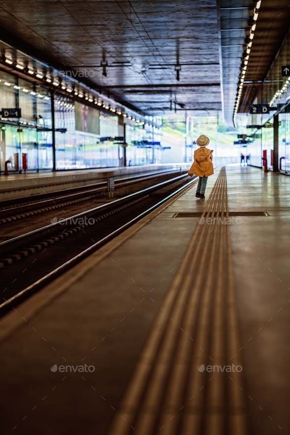 Back view of little child standing alone at empty railway station ...