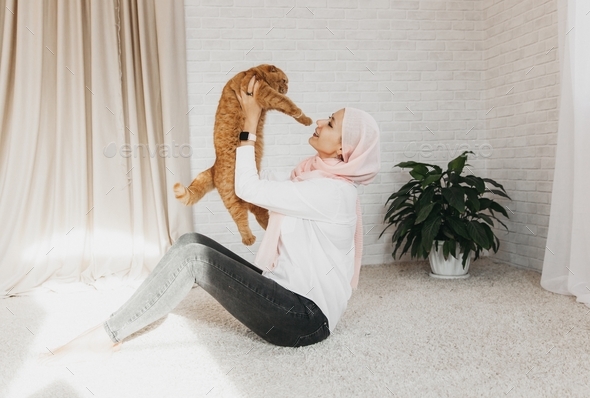 Young Muslim woman in hijab sits on the floor of the house and plays ...
