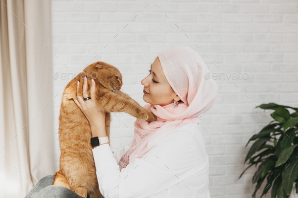 Young Muslim woman in hijab sits on the floor of the house and plays ...