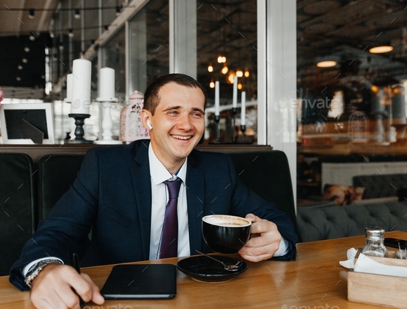 Handsome young businessman smiles and drinks coffee in a cafe. man in a ...