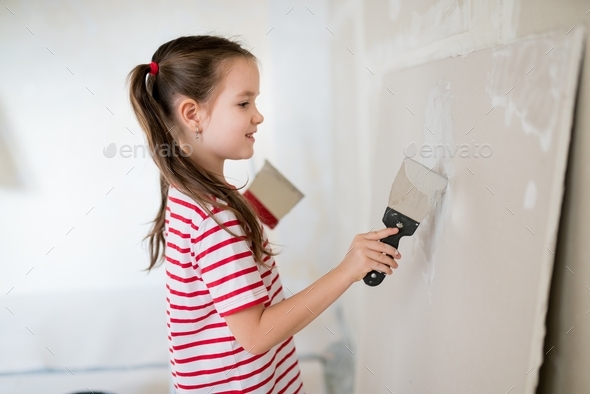 Child girl with trowel plastering a wall during house renovation ...