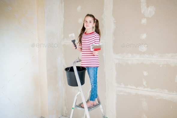 Child girl with trowel plastering a wall during house renovation ...