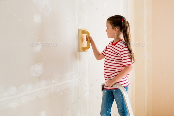 Child girl with trowel plastering a wall during house renovation ...